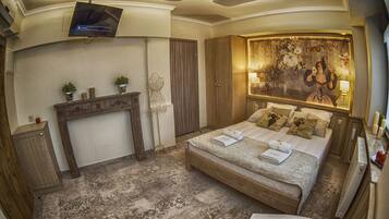 Quarto com uma cama grande, cômoda de madeira, lareira e televisão montada no teto.
