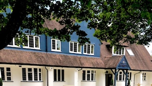 Um edifício com fachada azul, várias janelas e área externa coberta com cadeiras e mesas.