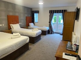 Quarto de hotel com três camas, uma escrivaninha de madeira, televisão e uma janela com cortinas.