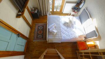 Quarto com cama, escrivaninha de madeira, cadeira, janela e escada.