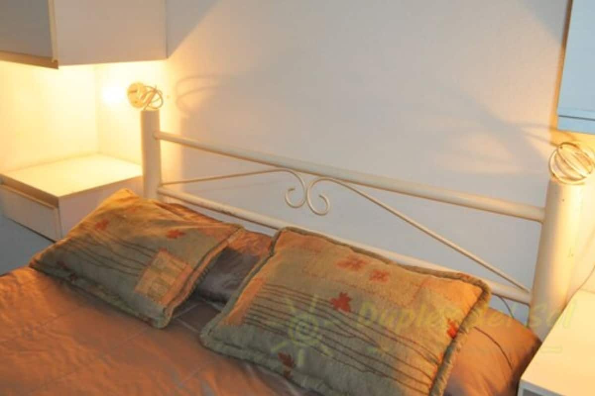 Uma cama com cabeceira de metal, duas almofadas e abajures.