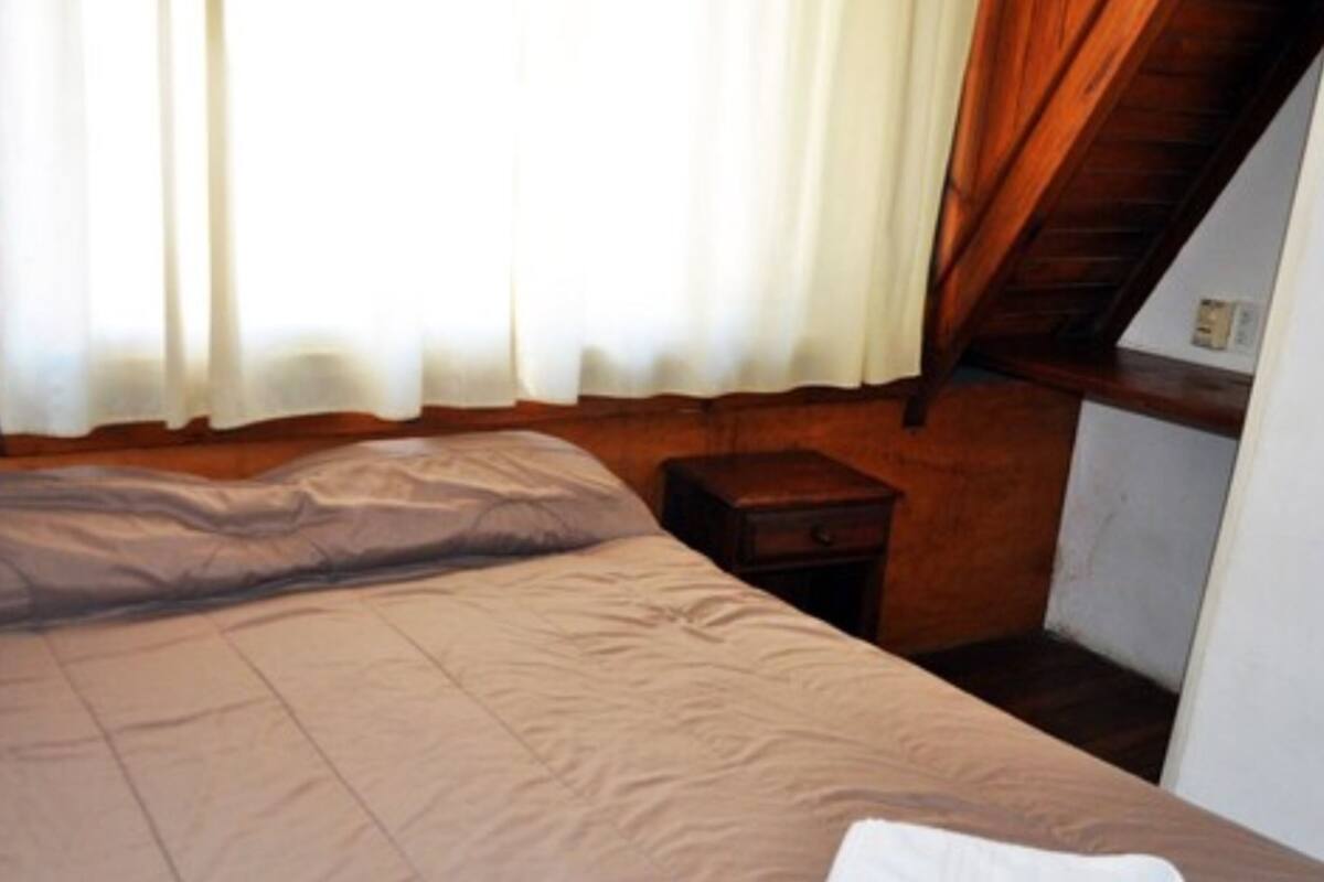 Quarto com cama, mesa de cabeceira e janela com cortinas.