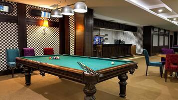 Uma mesa de bilhar com padrão quadriculado na parede, área de bar e diversas opções de assentos.