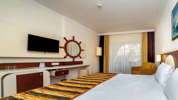 Quarto de hotel com uma cama grande, uma escrivaninha com televisão de tela plana, um espelho em formato de roda de navio, uma cadeira e uma janela com cortinas.
