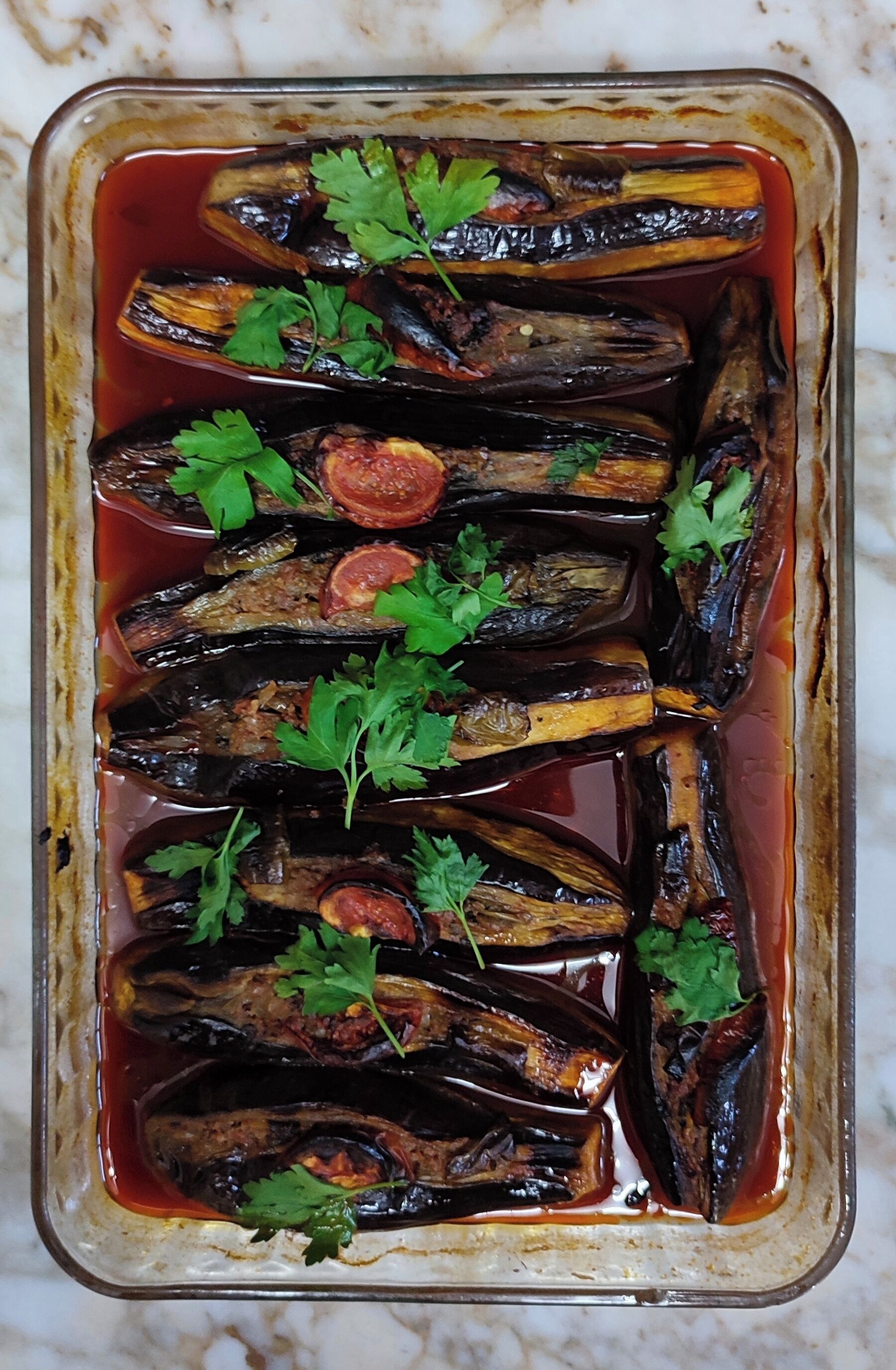 Uma travessa de vidro retangular com berinjelas assadas em molho vermelho, decorada com salsa.