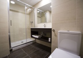 Uma casa de banho moderna com chuveiro envidraçado, sanita branca e lavatório escuro com espelho em cima.