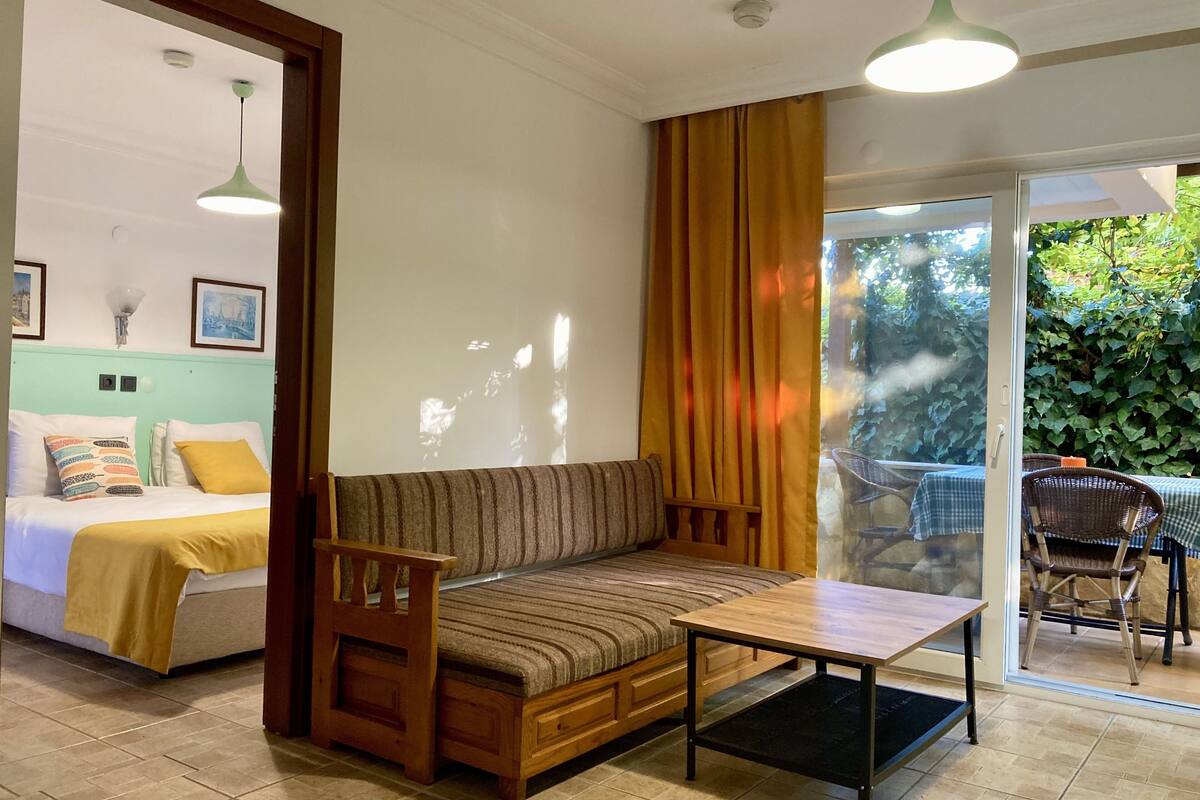 Um quarto aconchegante com uma cama, um sofá, uma mesinha e vista para o verde lá fora.