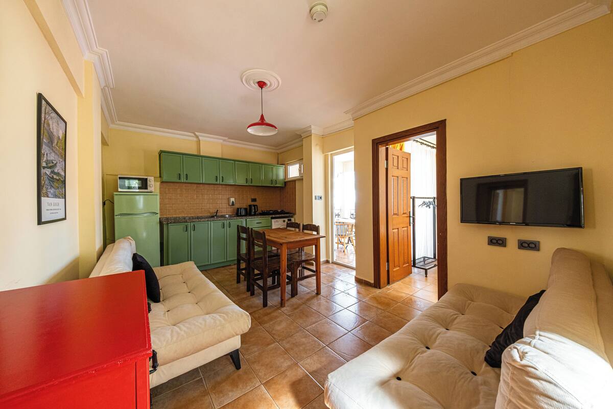 Um espaço compacto com cozinha compacta, área de jantar e sala de estar, incluindo um armário vermelho e dois sofás.