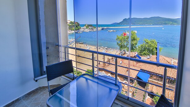 Uma varanda com vista para a praia e o mar, uma cadeira e uma mesa.