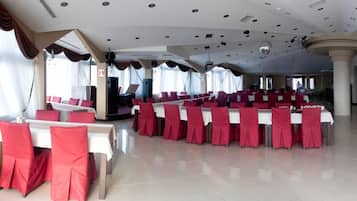 Um amplo salão de banquetes com fileiras de mesas e cadeiras, palco e design moderno no teto.