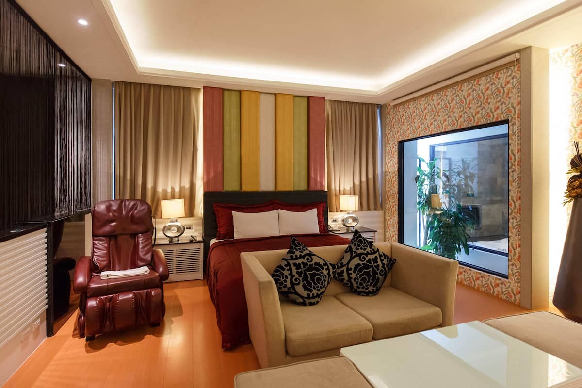 Quarto de hotel com cama, poltrona de massagem, sofá e uma janela grande com vista.