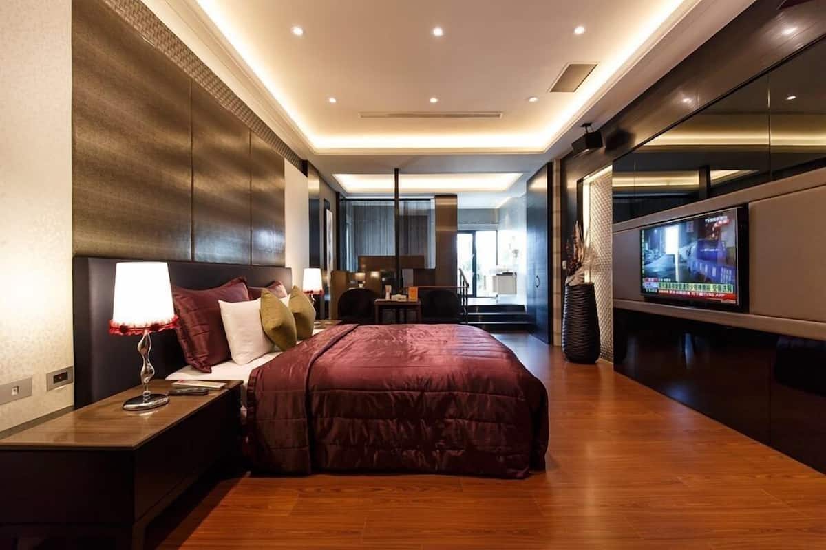 Quarto de hotel moderno com uma cama grande, uma TV e uma escrivaninha com abajur.