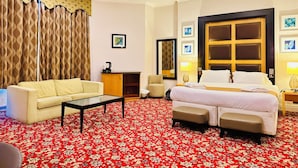 Quarto de hotel com uma cama grande, um sofá, uma mesa de centro, uma escrivaninha e um tapete floral vermelho.