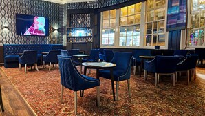 Um hall de hotel com parede estampada, televisão, poltronas estofadas em azul e carpete com padrão.
