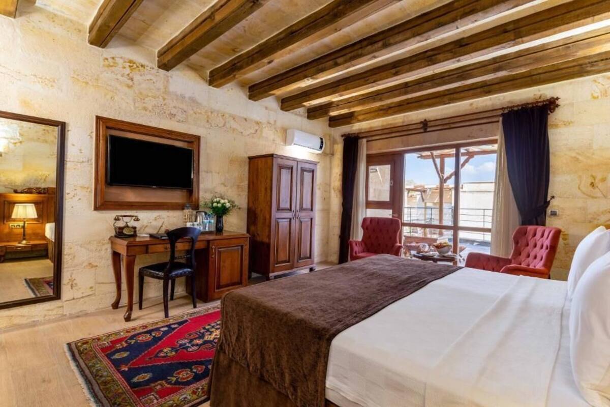 Quarto com cama, escrivaninha, cadeira, televisão e janela com cortinas.