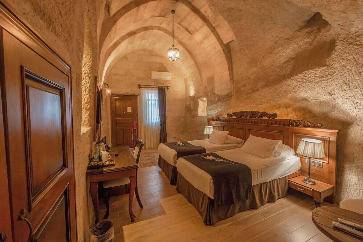 Quarto com duas camas, uma escrivaninha, uma cadeira, um abajur e cabeceira de madeira.