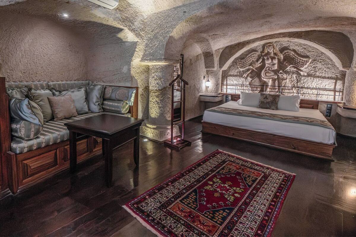 Um quarto acolhedor com teto de pedra, cama com colcha estampada, um banco de madeira e um tapete vermelho.