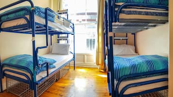 Quarto em dormitório com beliches, piso de madeira e janela com cortinas.