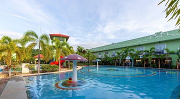 Piscina com escorrega, palmeiras e um edifício com fachada verde.