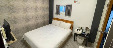 Quarto de hotel com cama, televisão, mesa de cabeceira com telefone e luminária, e janela com cortinas.