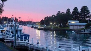 Uma marina com barcos atracados, um pequeno edifício e árvores ao fundo.