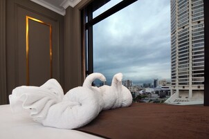 Arranjo de toalha em formato de cisne sobre uma cama, vista da cidade através de uma janela.