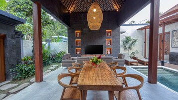 Uma área externa moderna com uma mesa de jantar de madeira, sofás e uma televisão.