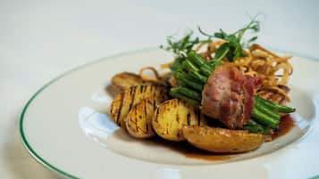 Um prato com batatas grelhadas, vagem e um pedaço de bacon.