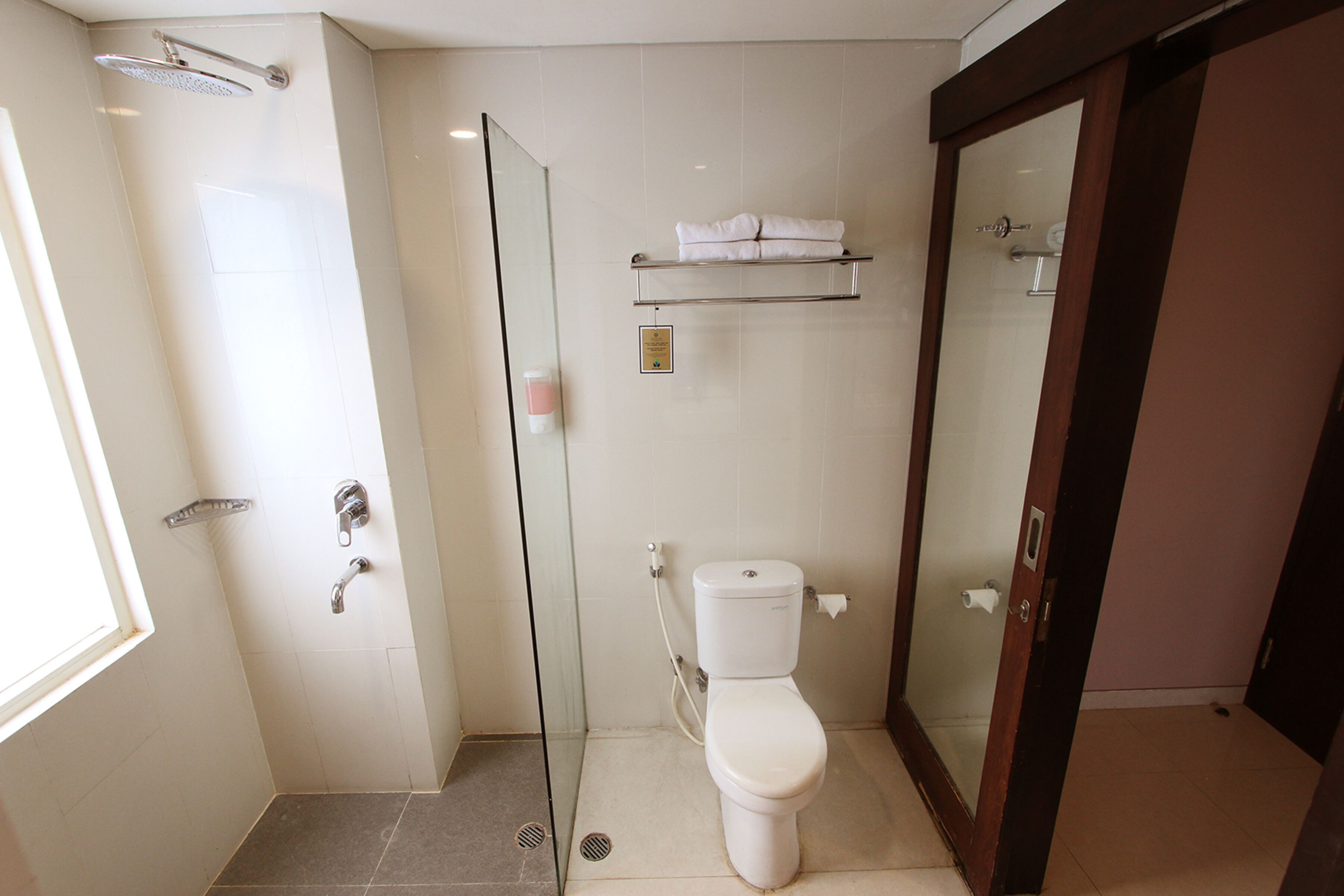 Uma casa de banho moderna com cabine de duche em vidro, sanita e prateleira com toalhas.