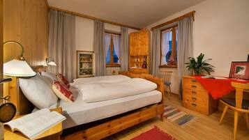 Quarto aconchegante com cama de madeira, mesa de cabeceira com abajur, cômoda e janela com cortinas.