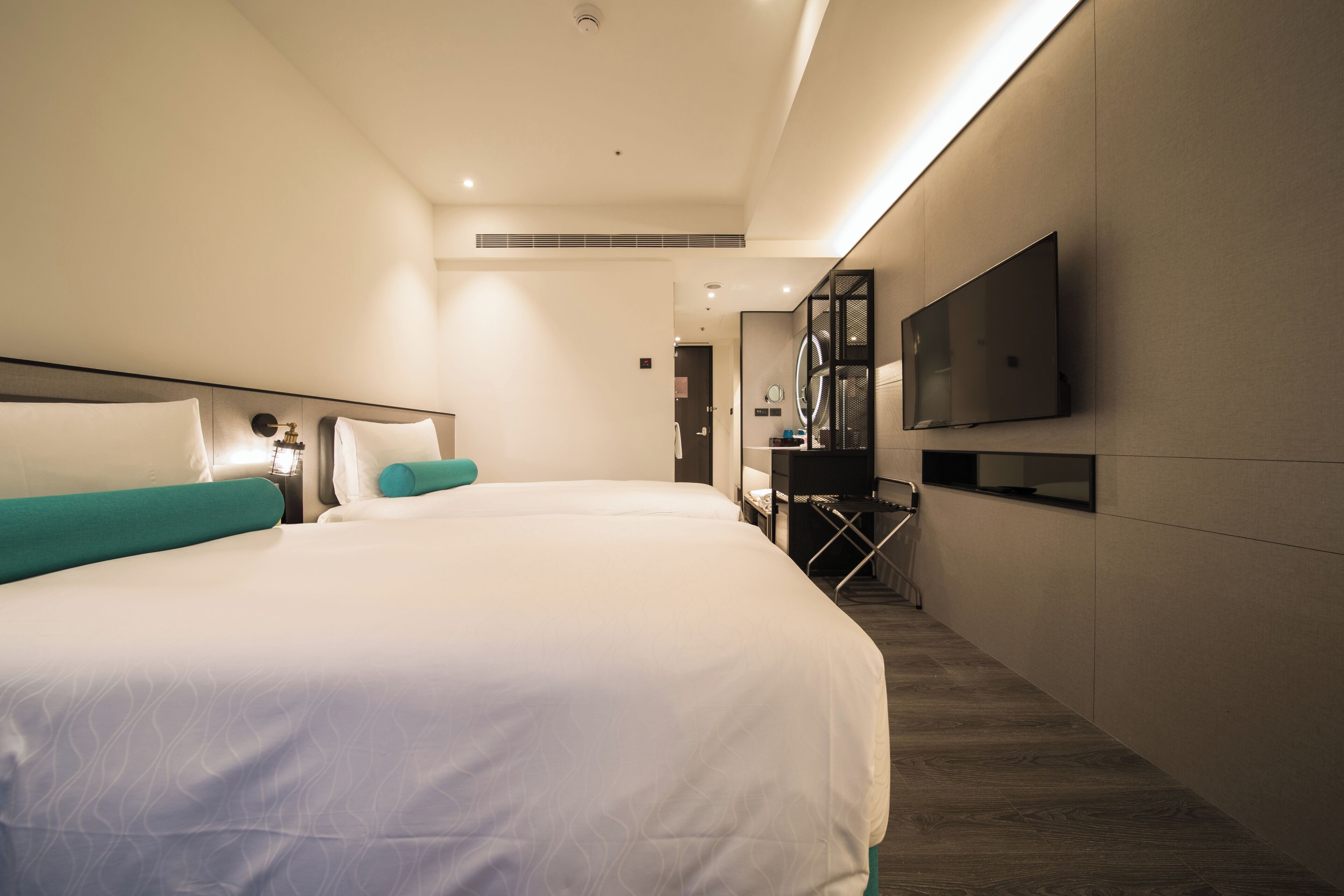 Quarto de hotel com duas camas, televisão fixada na parede e escrivaninha com cadeira.