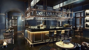 Uma área de bar com um barman, banquetas e um suporte para copos de vinho.