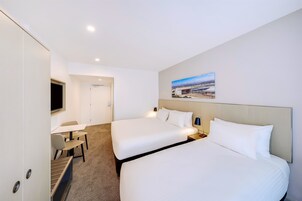 Quarto de hotel com duas camas, uma escrivaninha e uma cadeira.