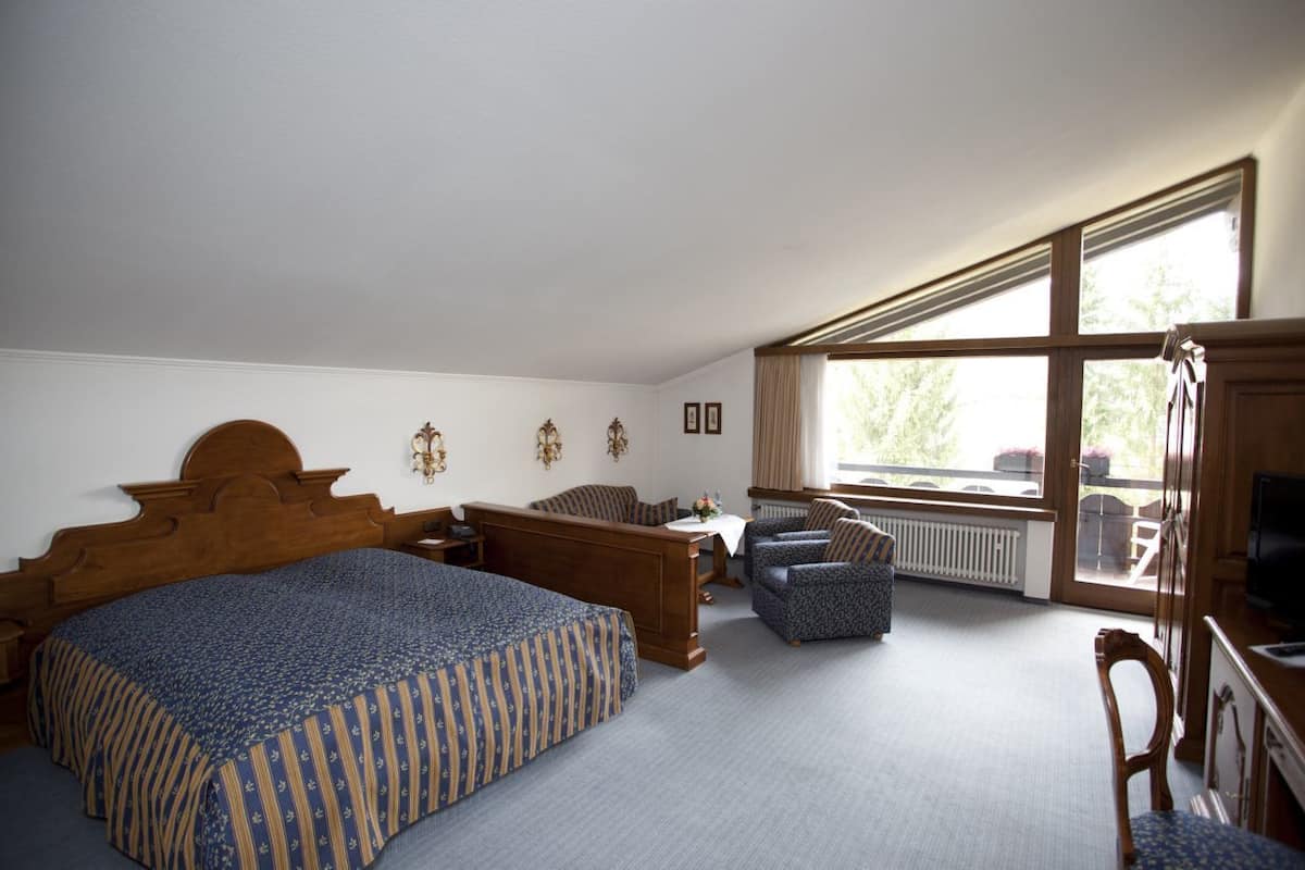 Quarto de hotel com uma cama grande, uma escrivaninha, uma cadeira e uma janela com vista para o exterior.