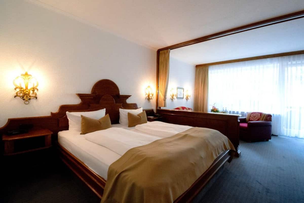 Quarto de hotel com uma cama grande, mesas de cabeceira, cômoda, espelho e uma janela com cortinas.