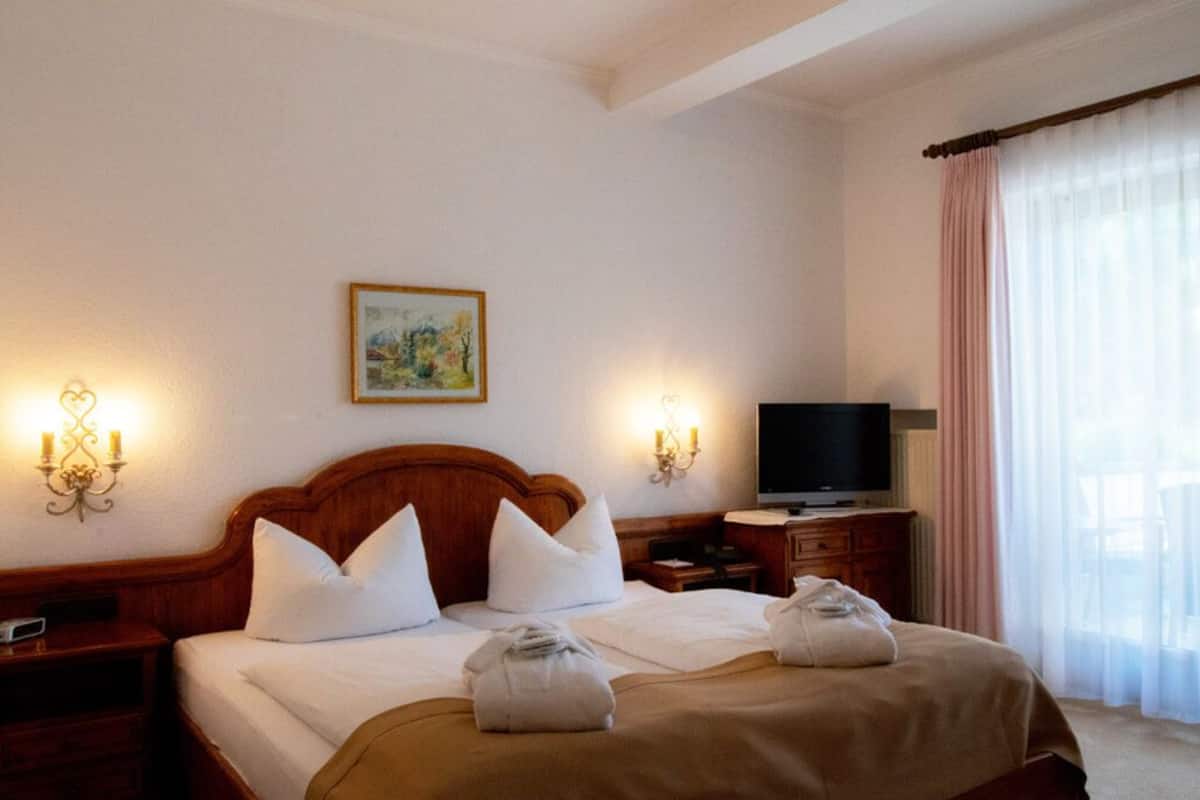 Quarto de hotel com cama de madeira, roupa de cama branca, televisão de tela plana e um quadro na parede.