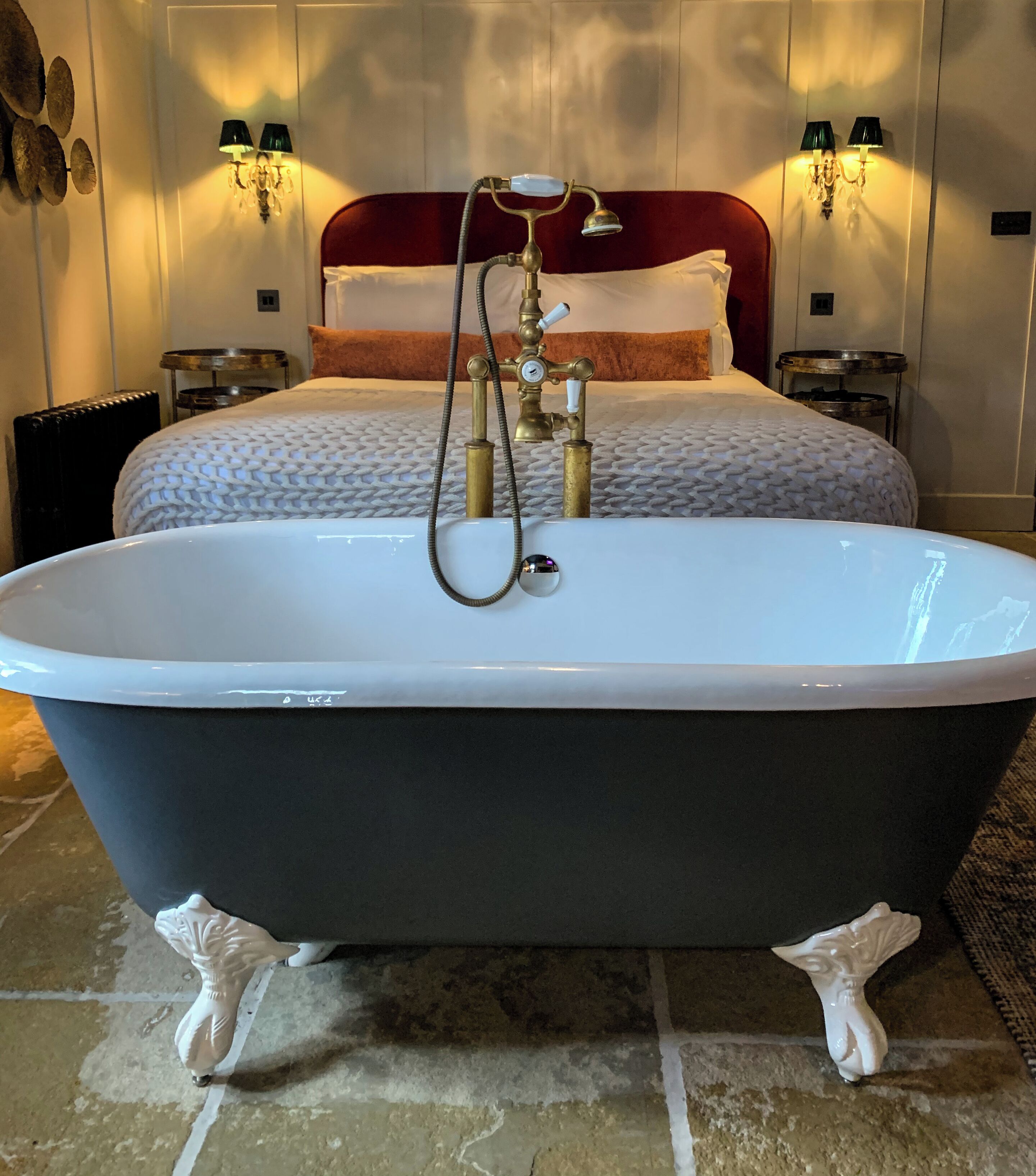 Quarto com uma banheira grande, cama com cabeceira vermelha e duas luminárias fixadas na parede.