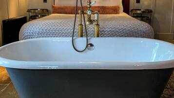 Quarto com uma banheira grande, cama com cabeceira vermelha e duas luminárias fixadas na parede.