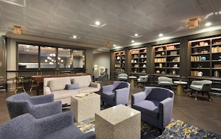 Uma área de estar moderna com sofás, poltronas e uma estante repleta de livros.