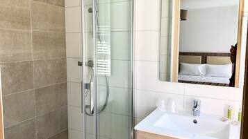 Uma casa de banho moderna com cabine de duche em vidro, uma sanita branca e um espelho em cima.
