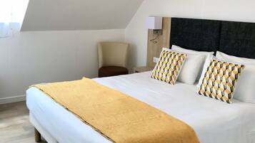 Um quarto moderno com teto inclinado, uma cama com lençóis brancos, um cobertor amarelo mostarda e almofadas estampadas.