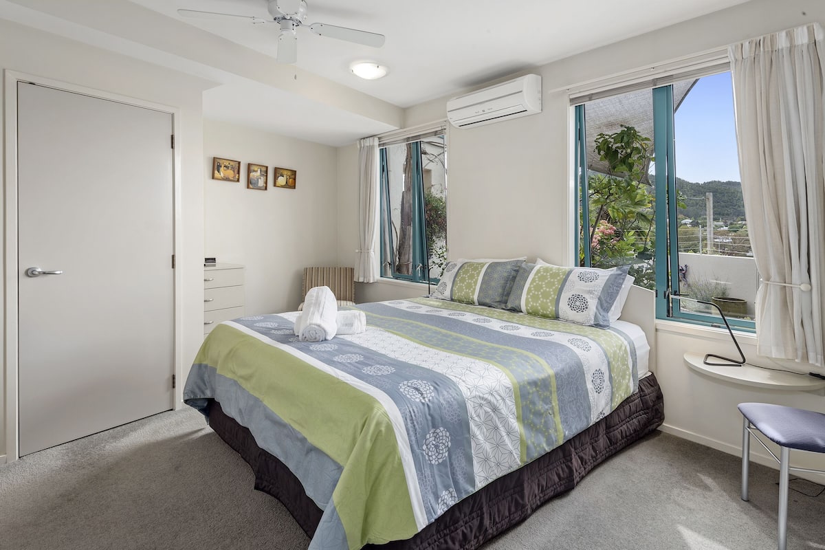 Quarto com cama, janela com vista, ventilador de teto e mesa de cabeceira.