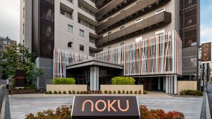 Um edifício moderno com uma placa de destaque 'noku', apresentando uma estrutura de vários andares com varandas e uma entrada central.