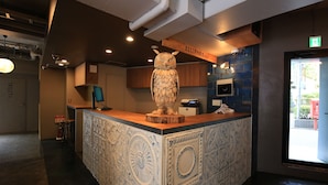 Uma mesa de recepção com uma escultura de coruja de madeira, um letreiro de recepção e vista para o exterior através de uma porta de vidro.