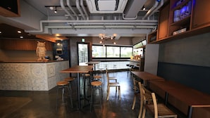 Um café moderno com um balcão central, diversas opções de assento incluindo banquetas e mesas, e uma grande janela que oferece luz natural.