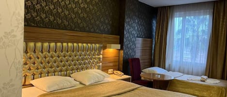Quarto de hotel com uma cama grande, mesa de cabeceira, uma cadeira e janela com cortinas.
