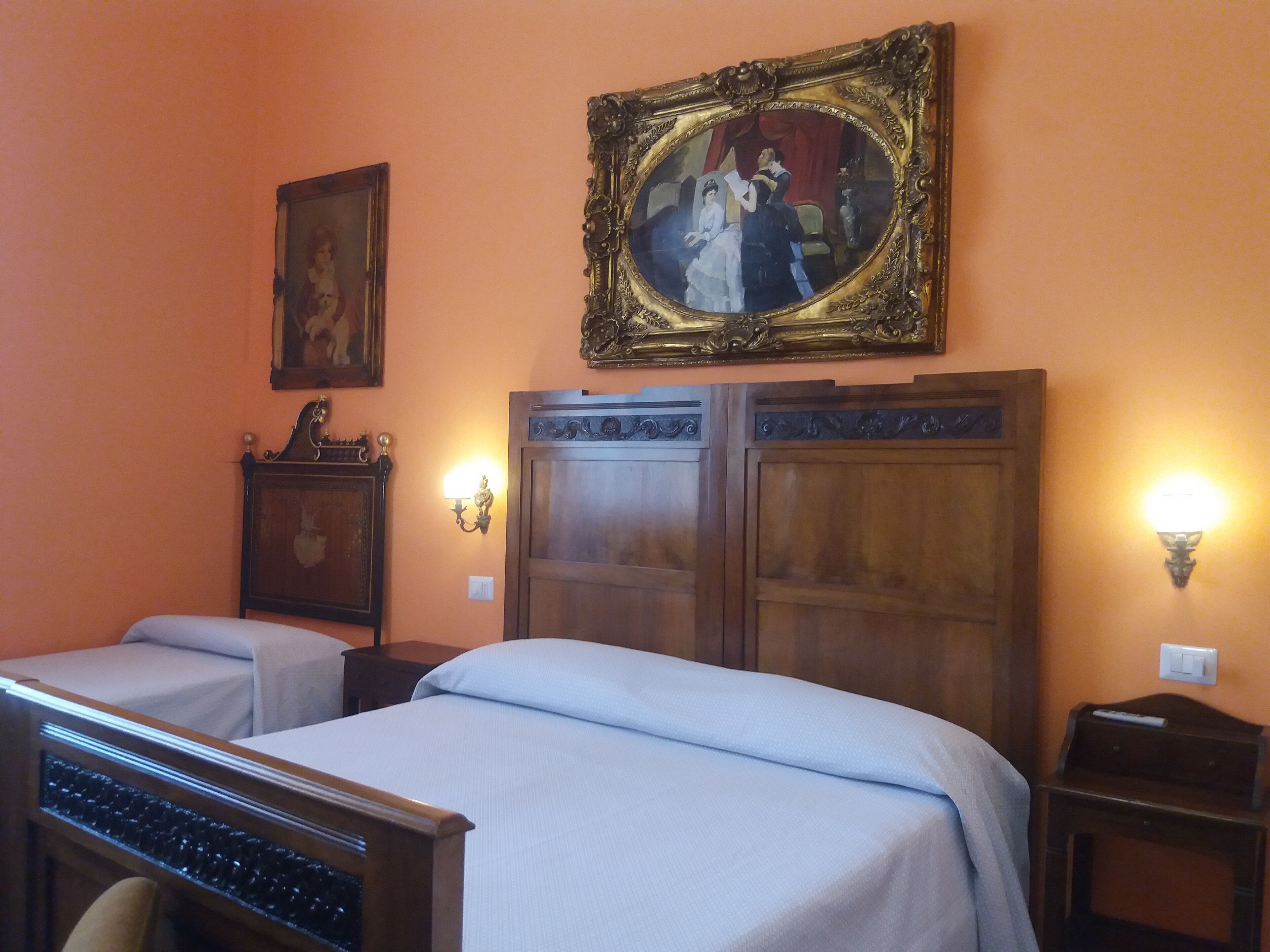 Quarto de hotel com duas camas, um guarda-roupa de madeira, um retrato emoldurado e luminárias fixadas na parede.