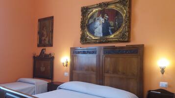 Quarto de hotel com duas camas, um guarda-roupa de madeira, um retrato emoldurado e luminárias fixadas na parede.