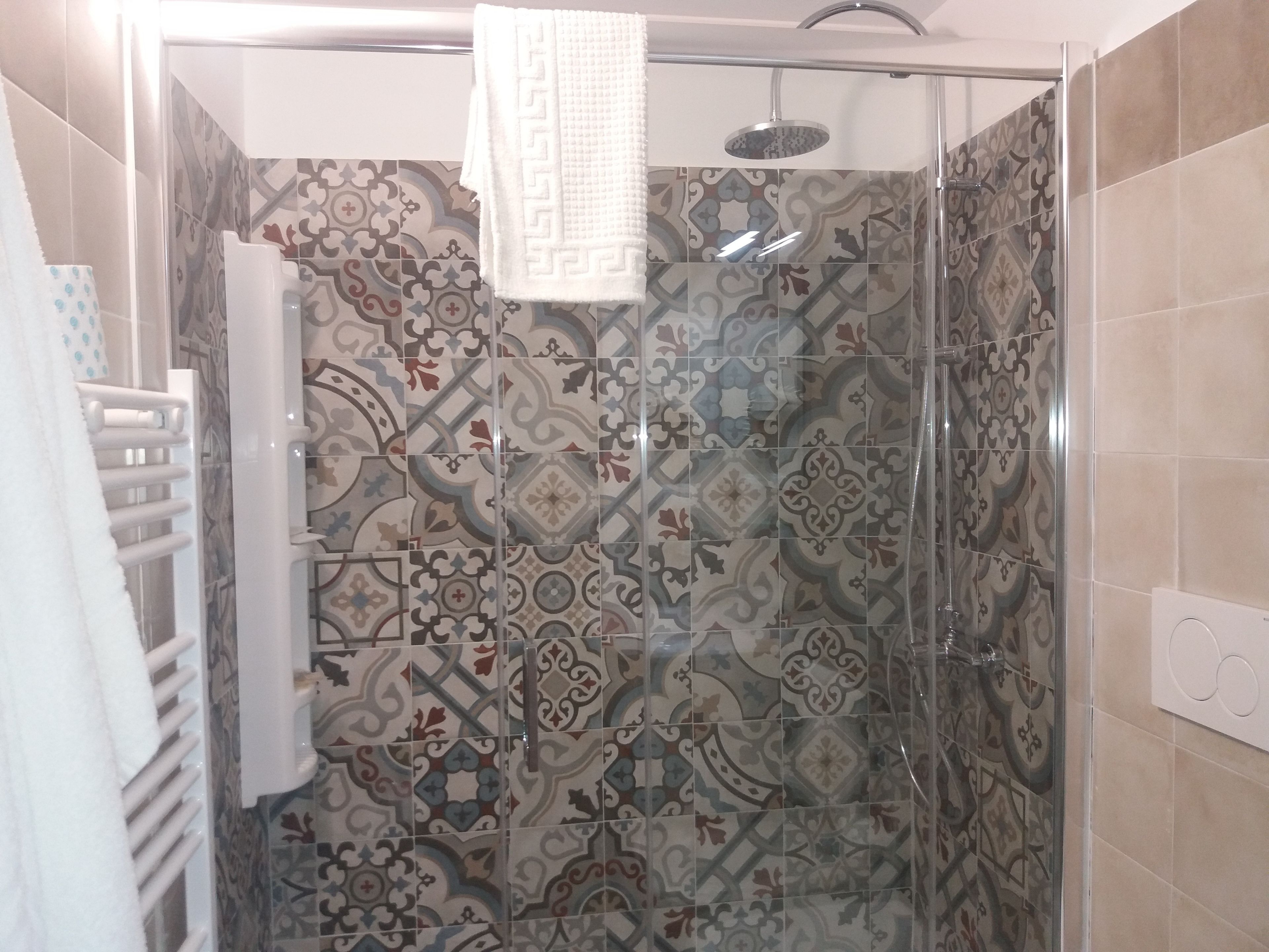 Chuveiro com porta de vidro, azulejos estampados e uma toalha branca pendurada na parede.