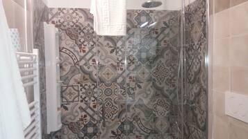 Chuveiro com porta de vidro, azulejos estampados e uma toalha branca pendurada na parede.
